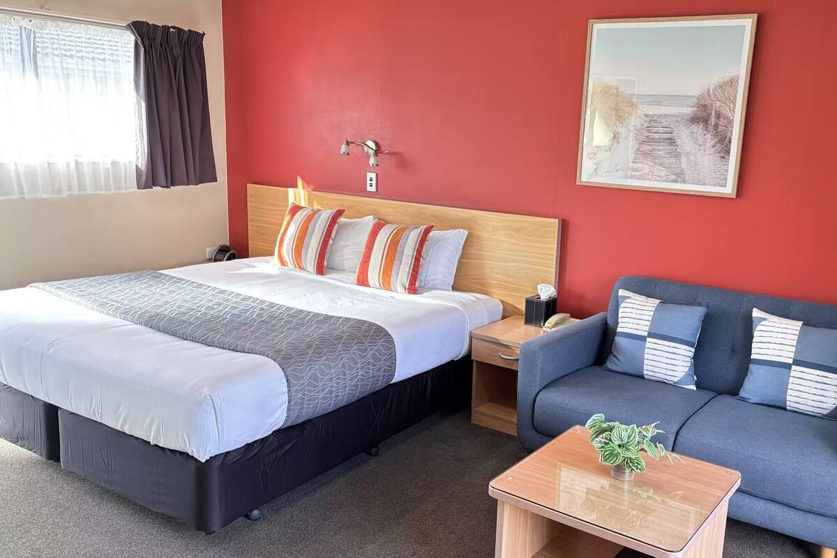 Quarto de hotel com cama, mesa de cabeceira, sofá e uma pequena mesa com uma planta.