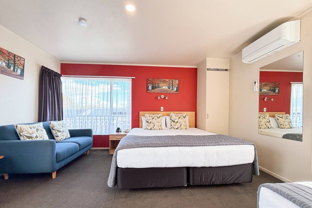 Quarto de hotel com cama, sofá azul, escrivaninha e uma janela grande.