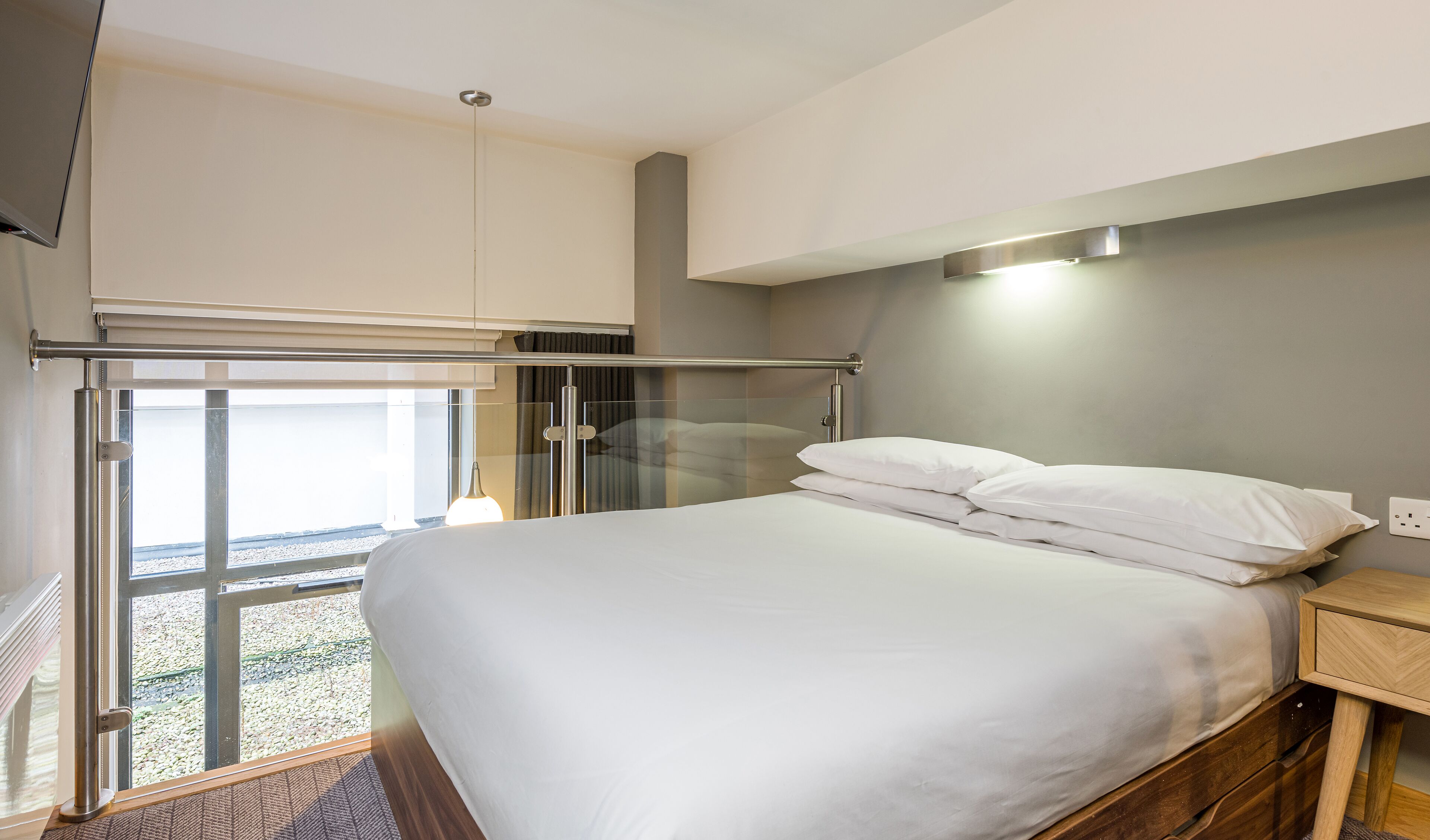 Quarto de hotel com cama, mesa de cabeceira, janela com vista para a praia e varanda com porta de vidro.