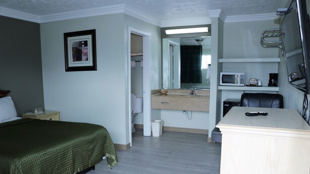 Quarto de hotel com cama, escrivaninha, cadeira, micro-ondas, espelho e televisão.