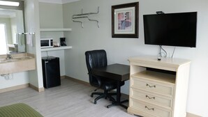 Quarto de hotel com cozinha compacta, escrivaninha, cadeira, televisão e cama.