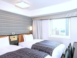 Quarto de hotel com duas camas, painel de controle, janela com vista para a cidade e uma luminária no teto.