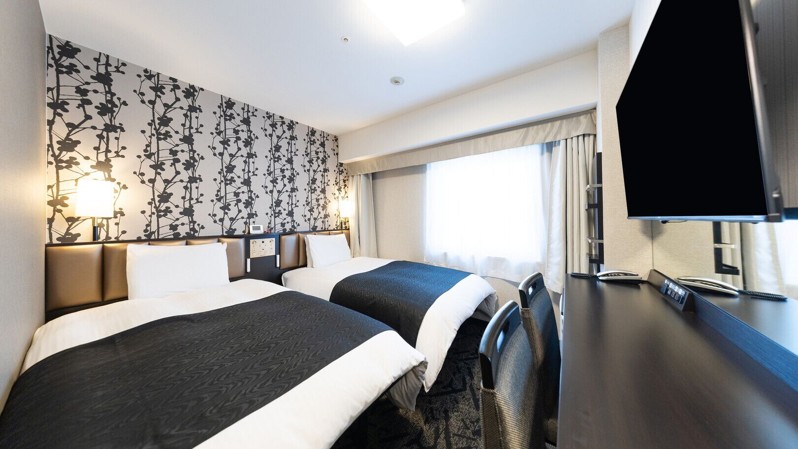 Quarto de hotel com duas camas, uma mesa com televisão de tela plana, telefone e luminária na parede.