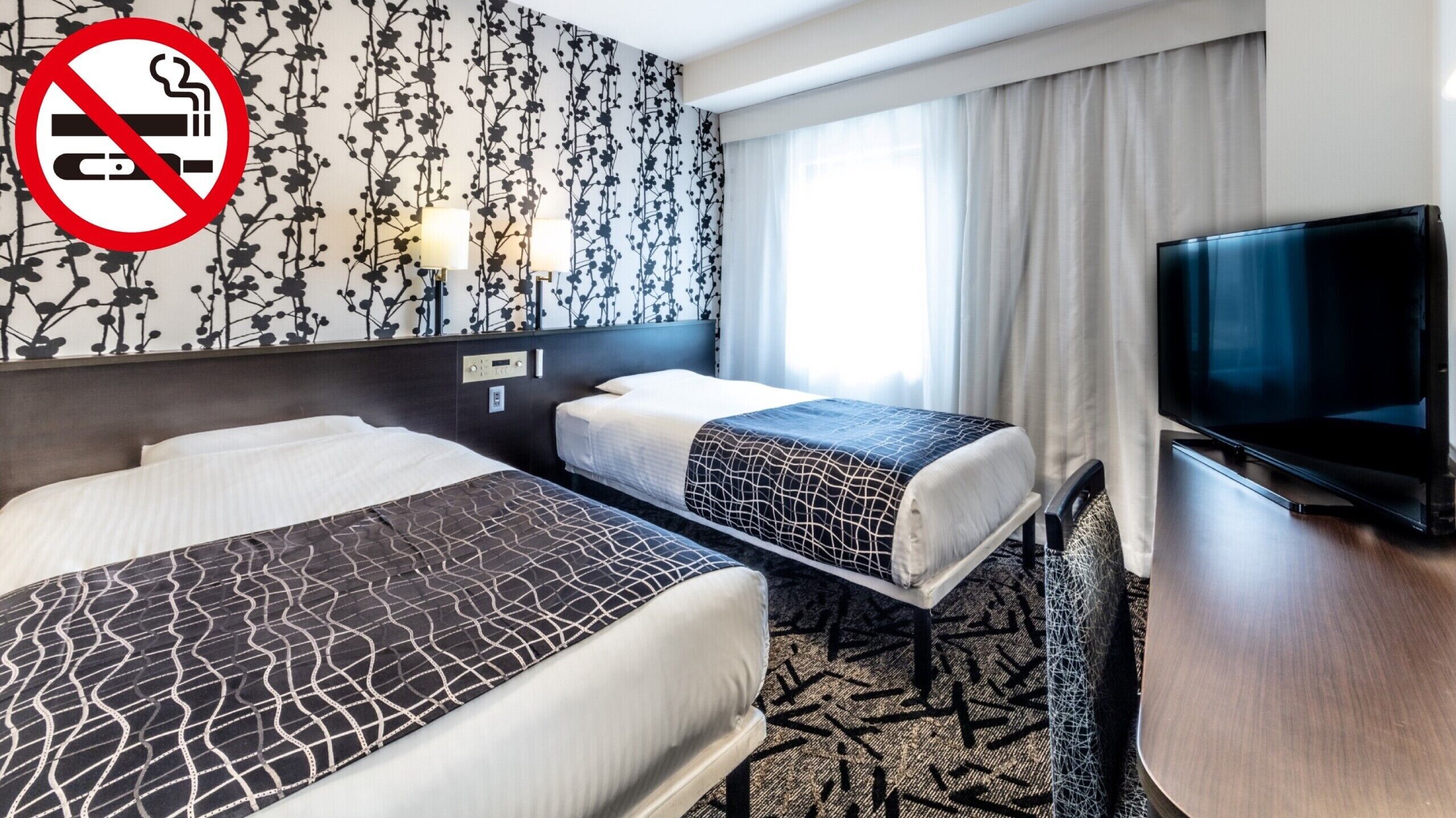 Quarto de hotel com duas camas, televisão e placa de 'não fumar'.