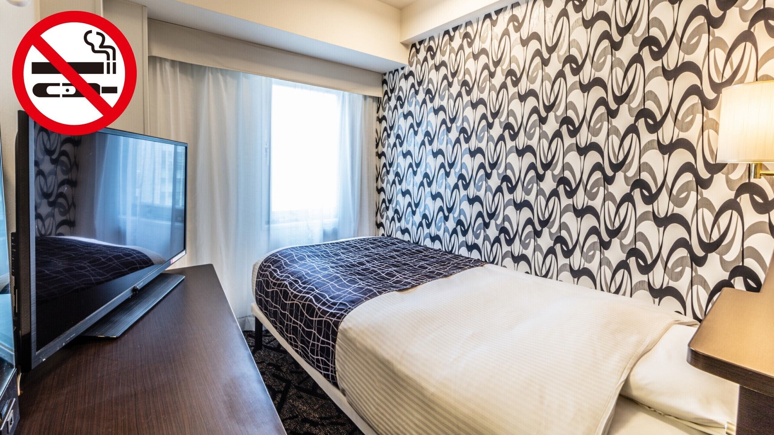 Quarto de hotel com cama, televisão sobre suporte, placa de proibido fumar e papel de parede estampado.