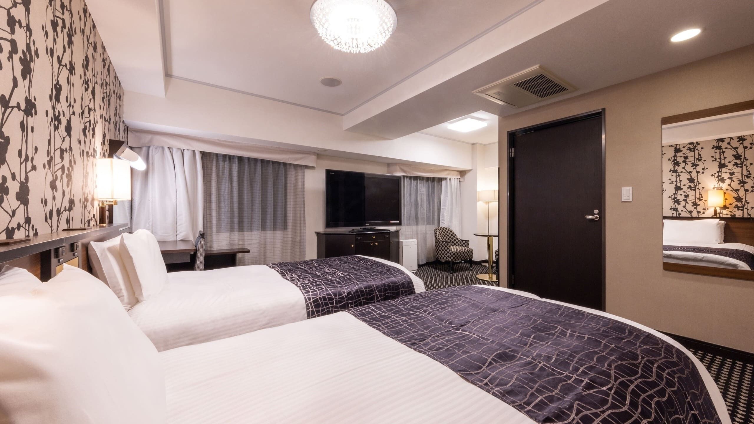 Quarto de hotel com duas camas, uma escrivaninha, uma televisão e uma porta.
