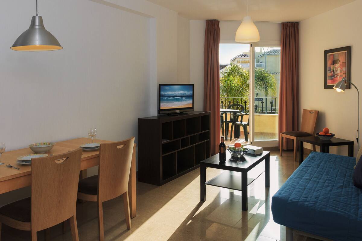 Sala de estar moderna com televisão, mesa de jantar, cadeiras e um sofá azul.