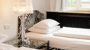 Quarto de hotel com duas camas, cabeceira estampada com padrão de zebra, radiador e janela com cortinas.