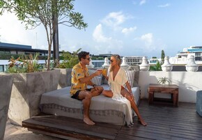 Um casal sentado em um sofá com vista para barcos e edifícios ao fundo.