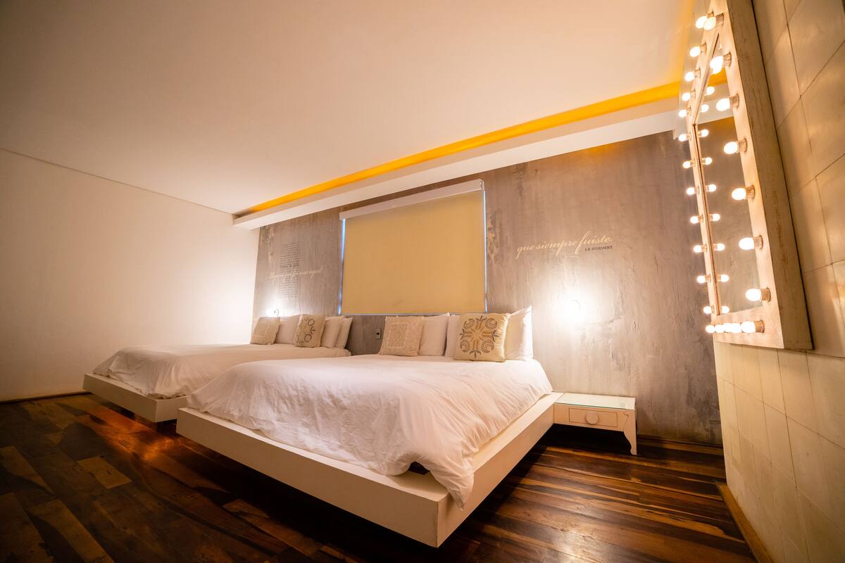 Quarto moderno com uma cama grande, toucador iluminado e piso de madeira.