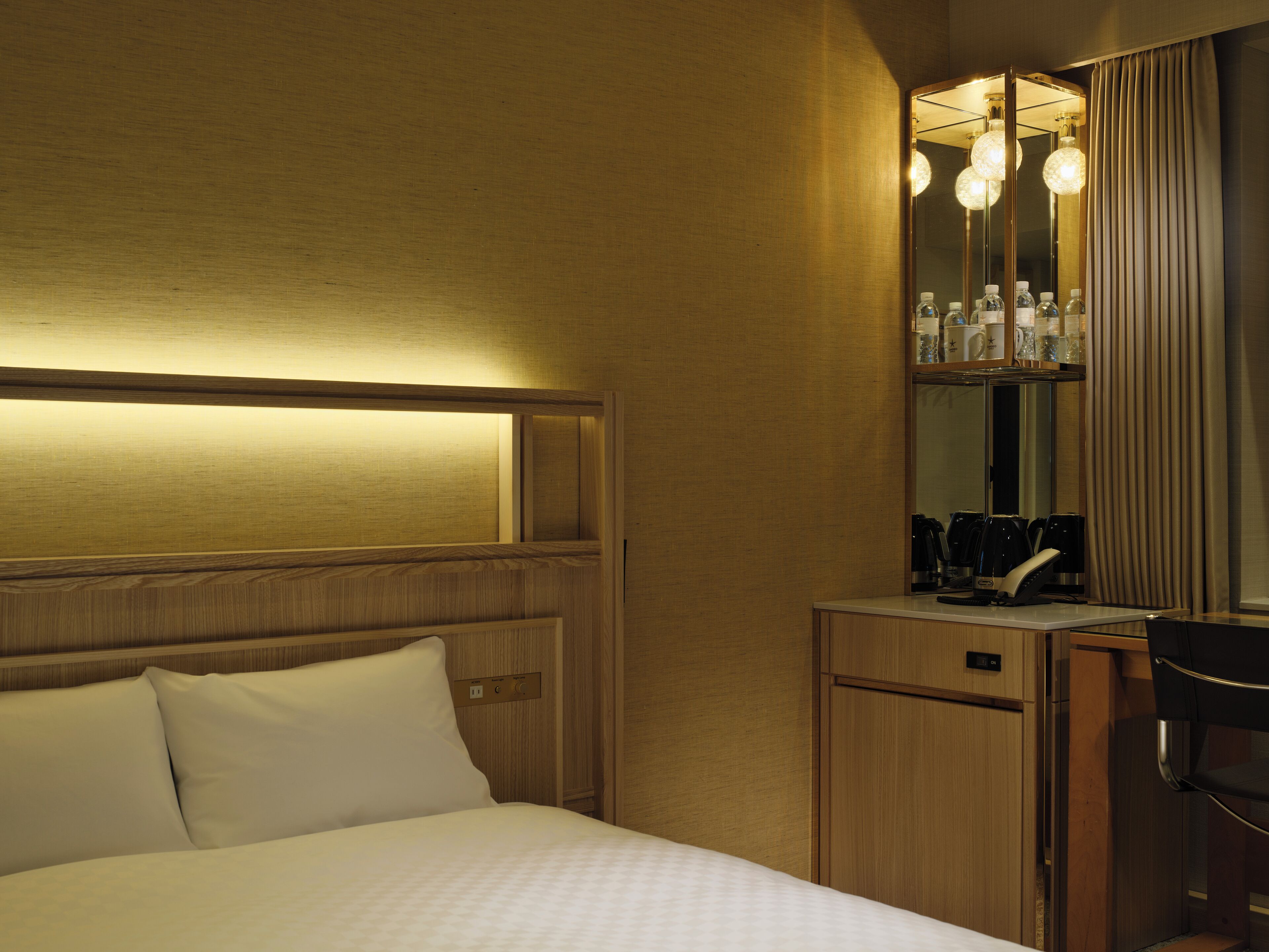 Quarto de hotel com cama, escrivaninha, espelho e minibar.