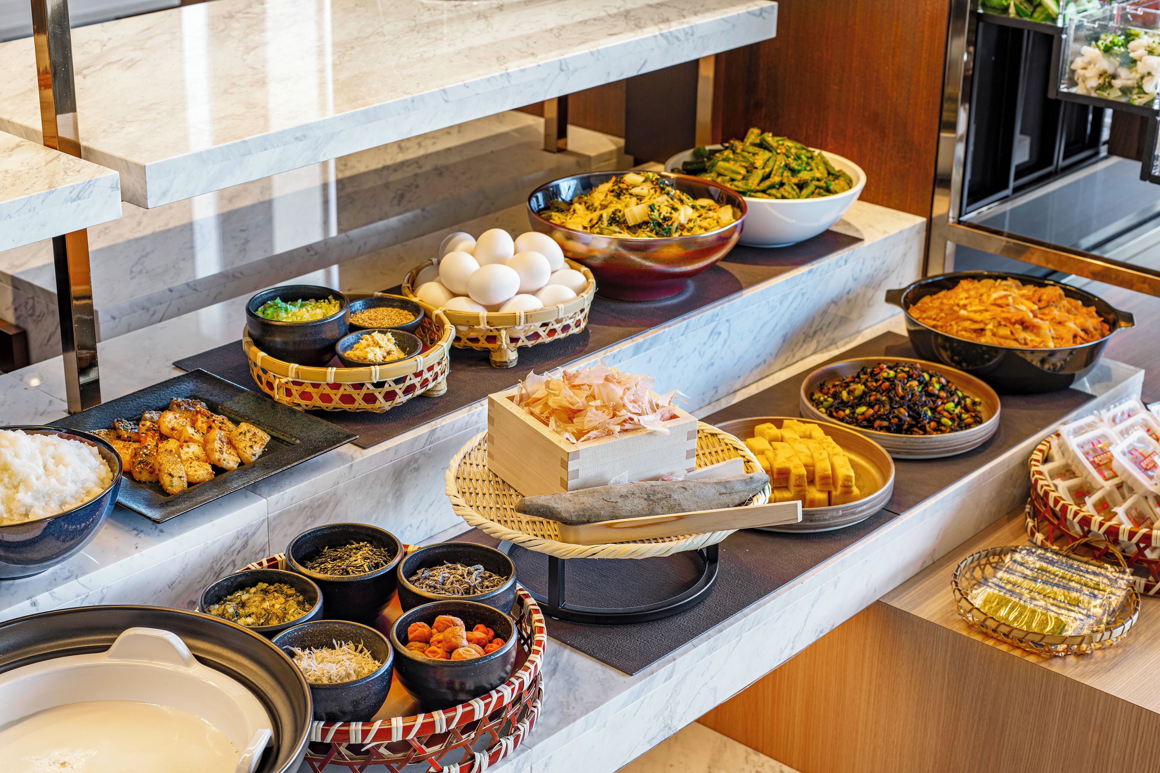 Buffet com diversos pratos e um bolo em um balcão de mármore.
