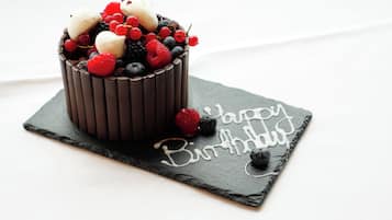 Bolo de chocolate com frutos vermelhos sobre uma tábua de ardósia com a mensagem 'Happy Birthday'.