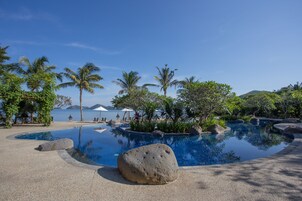 Área da piscina com vista clara para o mar, cercada por palmeiras e rochas.