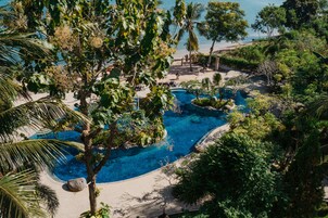 Piscina rodeada por vegetação exuberante e vista para a praia.