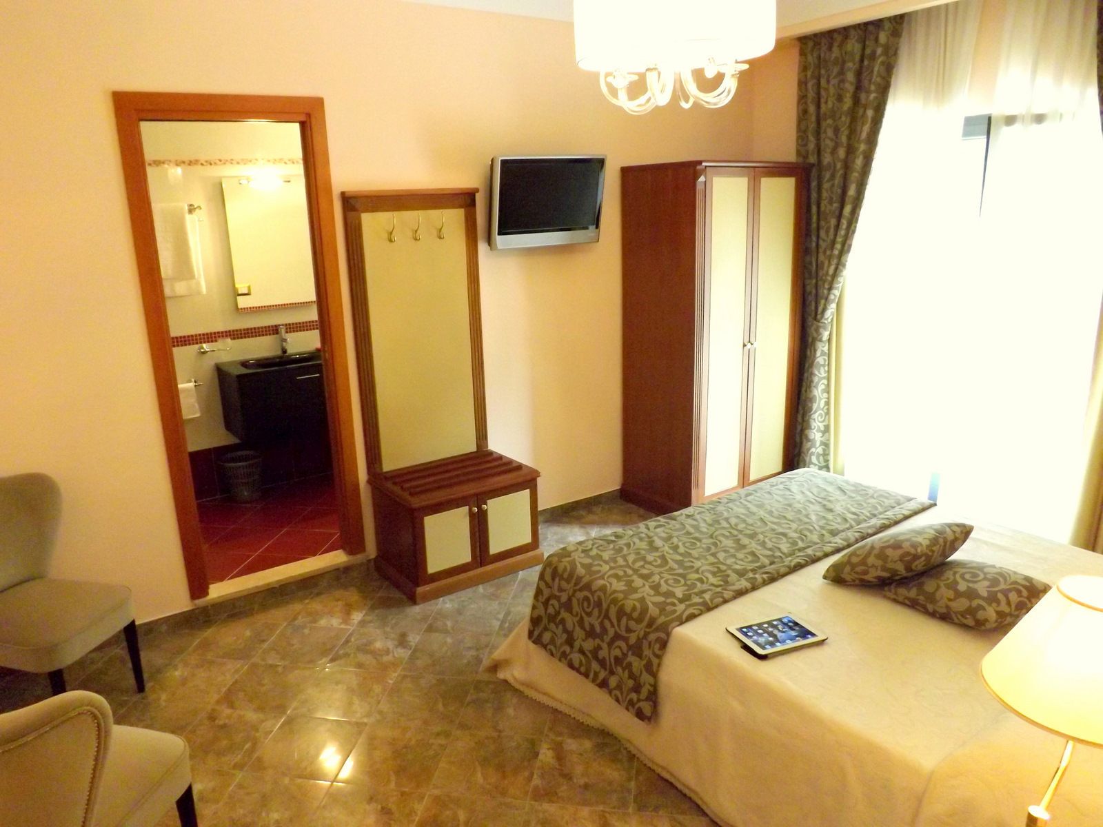Quarto de hotel com cama, televisão, guarda-roupa, espelho e uma cadeira.
