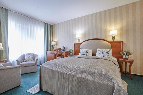 Quarto de hotel com uma cama grande, uma escrivaninha, uma cadeira e uma pequena mesa com abajur.