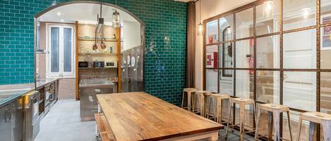 Cozinha moderna com paredes de tijolos azuis, eletrodomésticos de aço inoxidável e uma mesa de jantar de madeira com banquetas altas.
