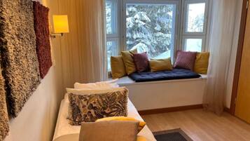Um quarto aconchegante com uma cama, um assento à janela com almofadas e vista para árvores cobertas de neve.
