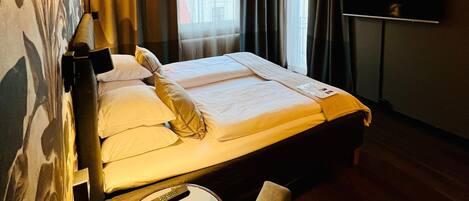 Quarto de hotel com cama, mesa redonda, uma cadeira, televisão e janela com cortinas.
