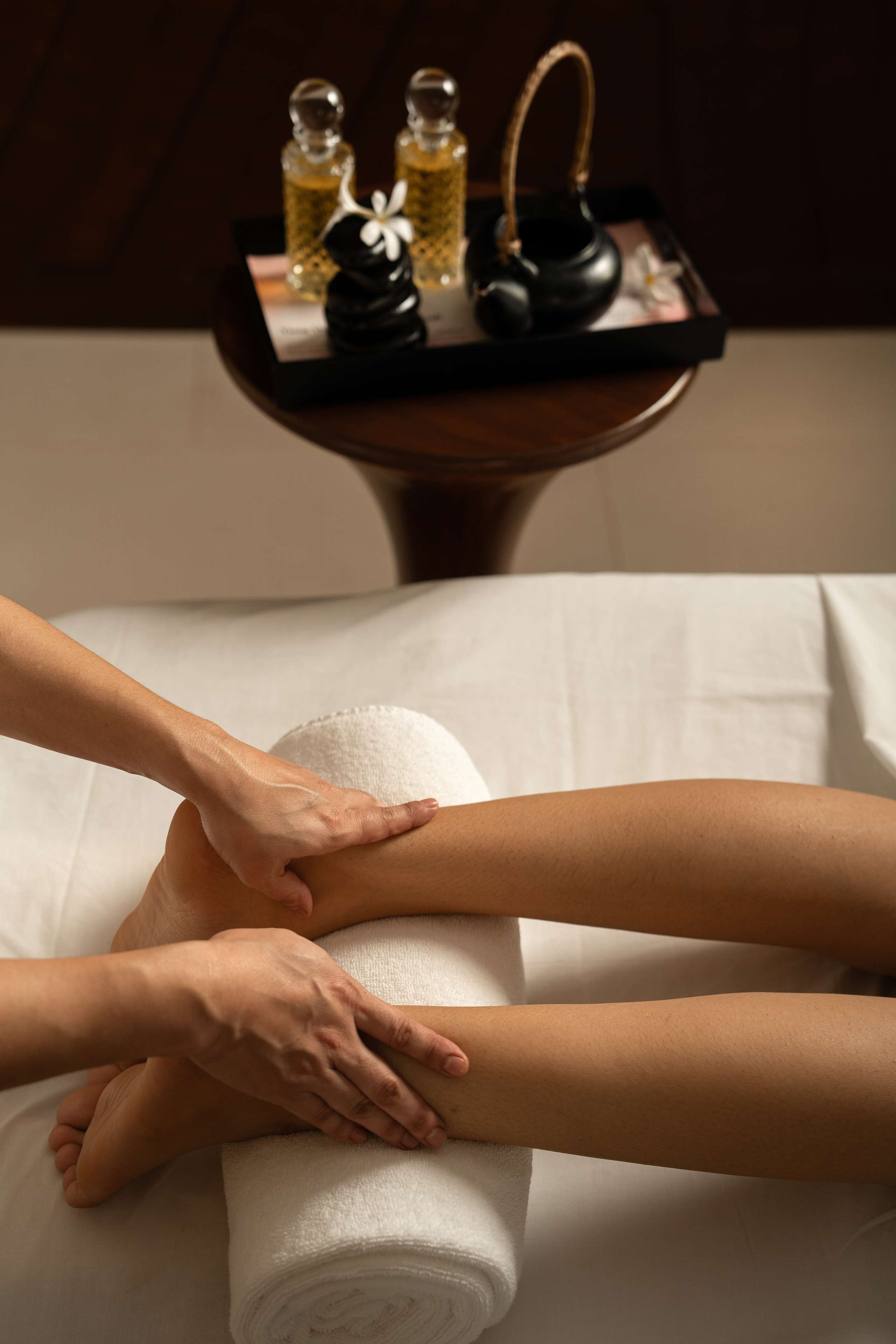 Sessão de massagem com uma toalha enrolada e uma bandeja com garrafas e um bule ao fundo.