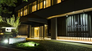 Entrada de hotel com placa de identificação, caminho bem iluminado e fachada de prédio moderna.
