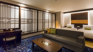 Quarto de hotel com sofá, escrivaninha, mesa de centro e cama com almofadas.