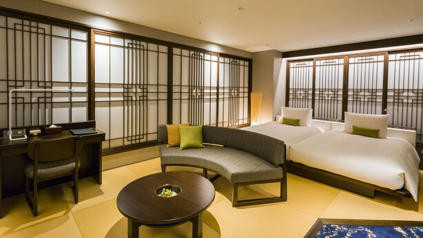 Quarto de hotel com sofá, duas camas, escrivaninha e uma mesinha.