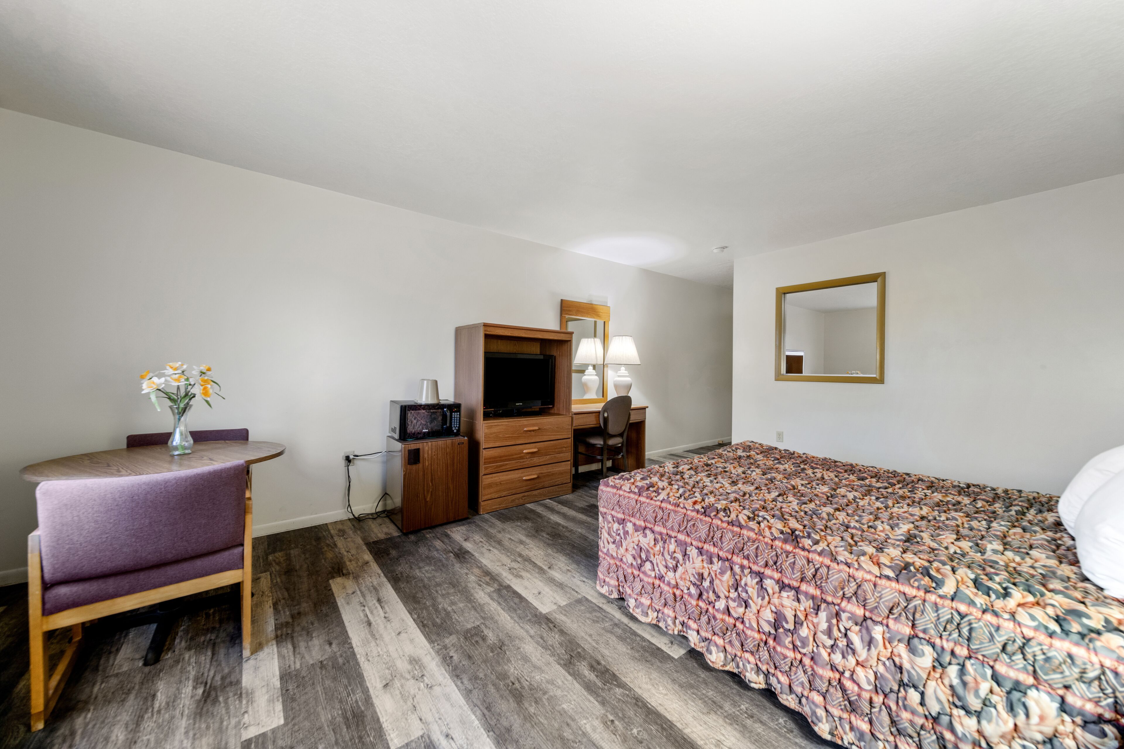 Quarto com uma cama, escrivaninha, cadeira, cômoda e televisão.