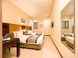 Quarto de hotel com duas camas, uma escrivaninha, uma cadeira, uma televisão e um espelho.