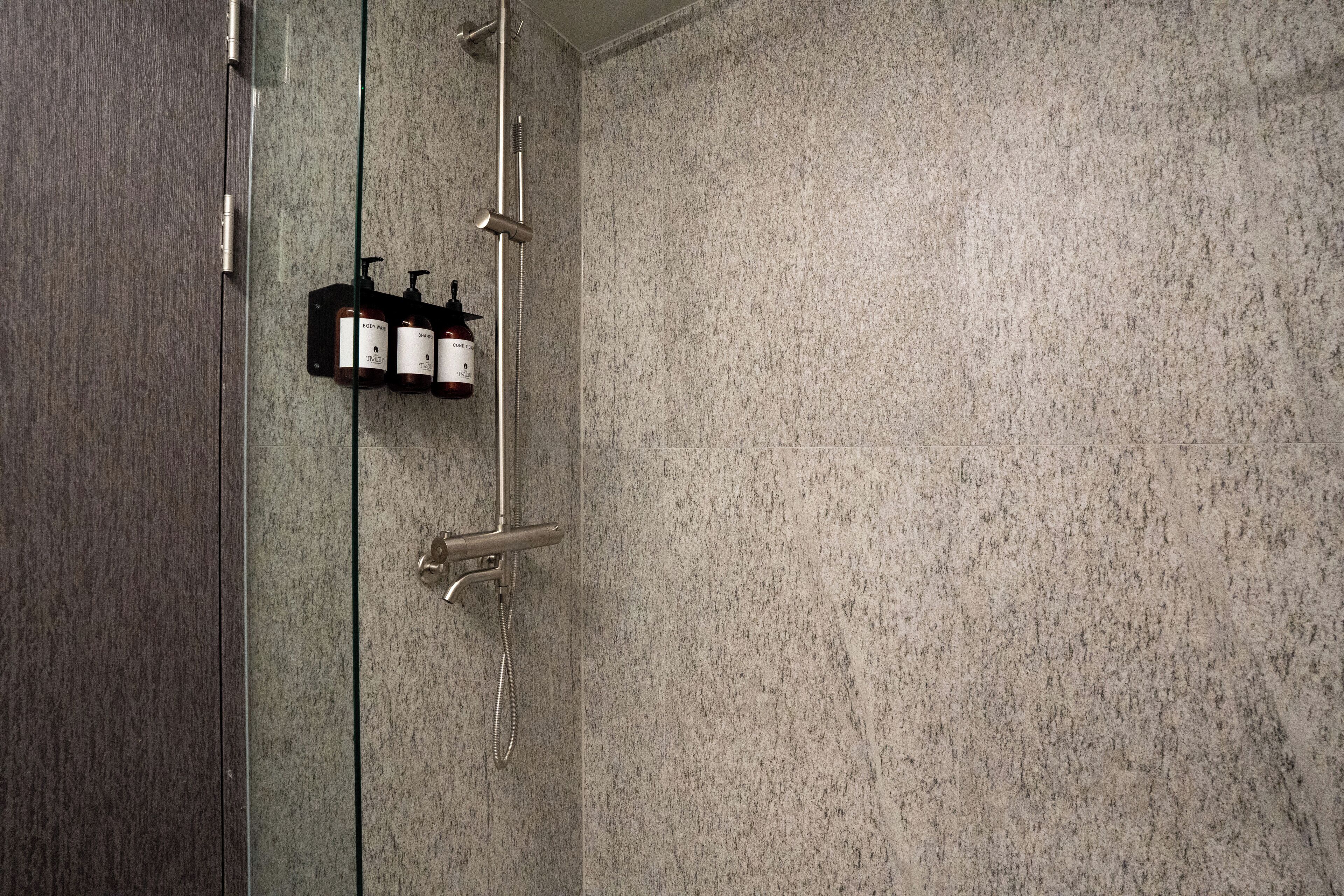 Chuveiro com porta de vidro, chuveiro manual e uma embalagem de shampoo.