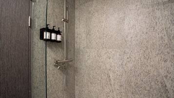 Chuveiro com porta de vidro, chuveiro manual e uma embalagem de shampoo.