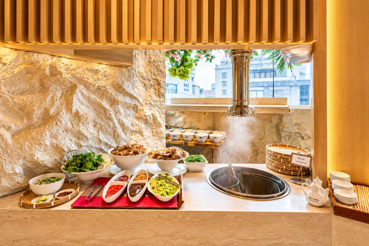 Disposição de buffet com diversos pratos, um caldeirão quente e um painel de parede de pedra.