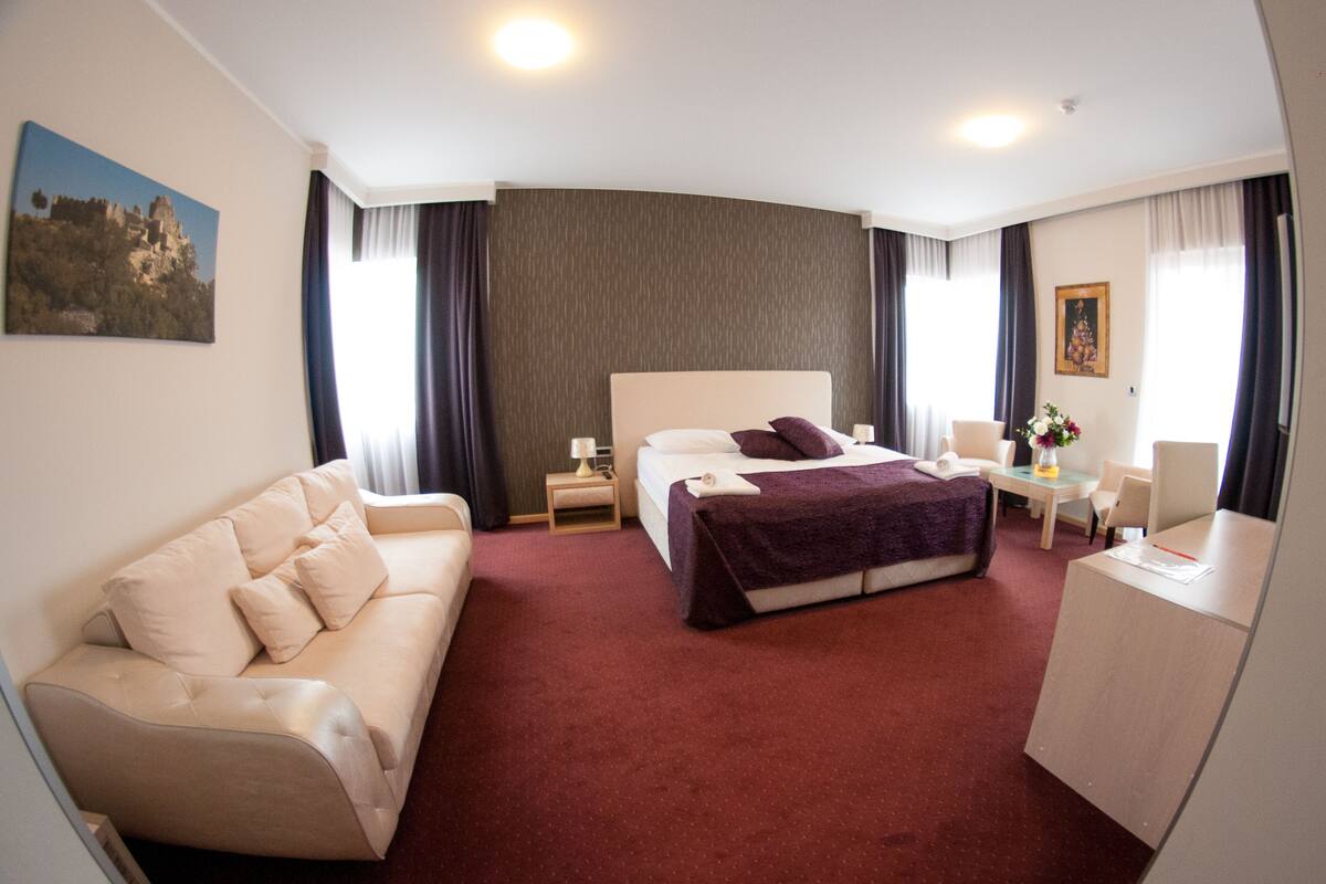 Quarto de hotel com uma cama grande, um sofá, uma escrivaninha e uma mesa de cabeceira.