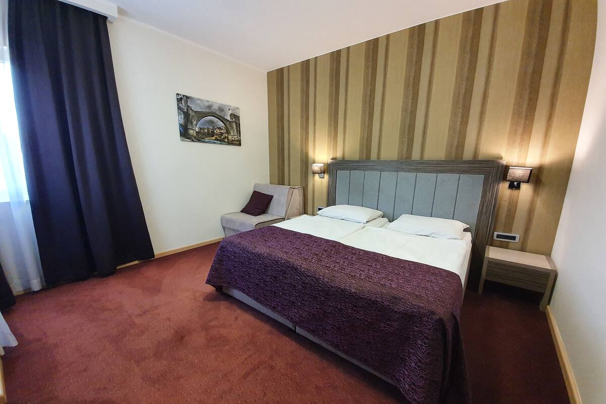 Quarto de hotel com uma cama grande, uma cadeira, um quadro na parede e um papel de parede listrado.
