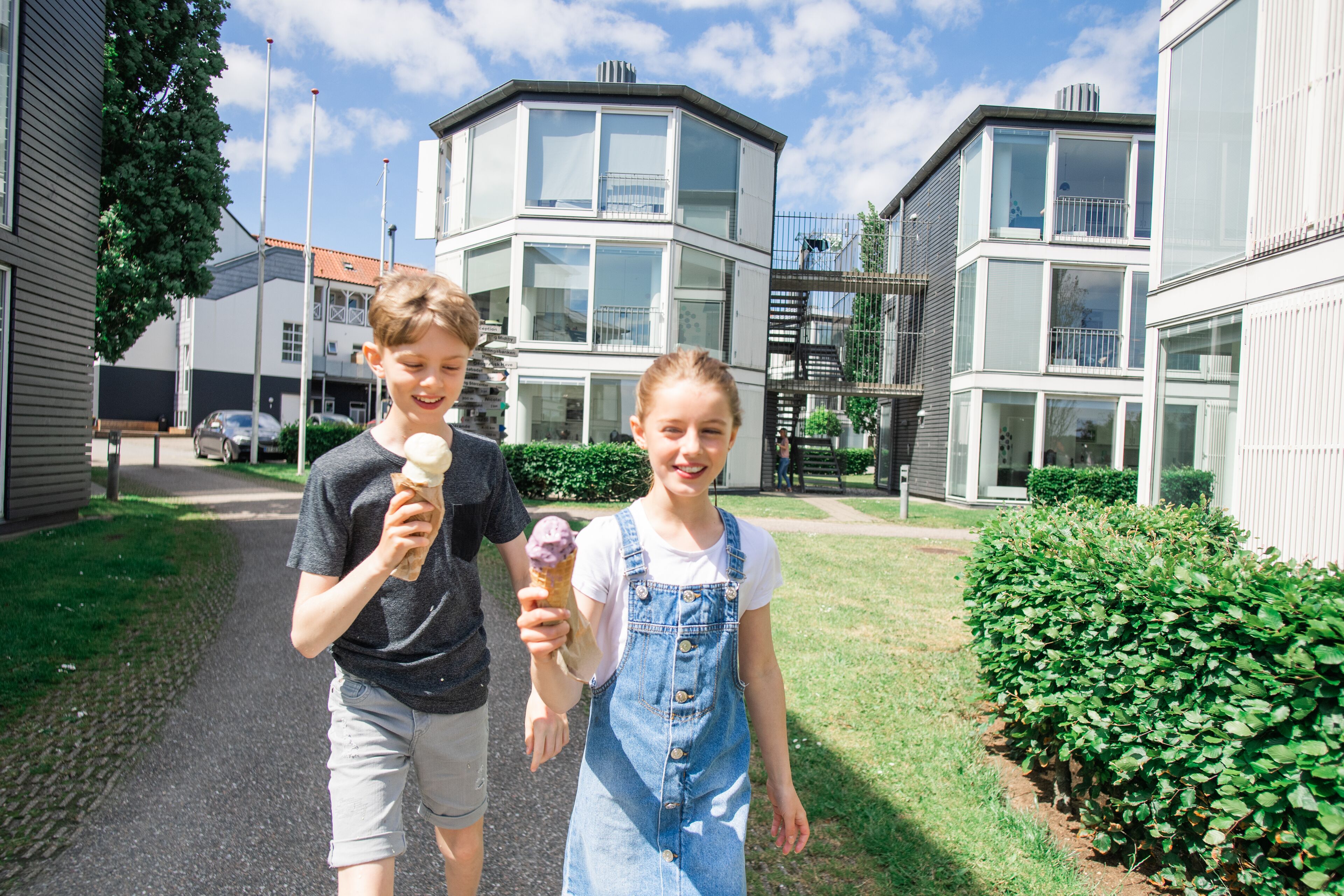 Duas pessoas caminham por um caminho, com edifícios modernos ao fundo.