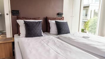 Quarto de hotel com duas camas, cada uma com roupa de cama branca e almofadas com padrão geométrico.