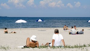 Uma praia com pessoas se bronzeando e relaxando sob guarda-sóis.