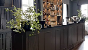 Uma área de bar com painéis de madeira escura, prateleiras cheias de garrafas e plantas em vasos.