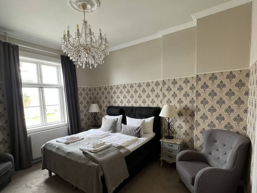 Quarto com cama, mesa de cabeceira, cadeira, lustre e papel de parede estampado.