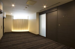 Um corredor de hotel com piso carpeteado, uma porta deslizante com o número 13 e iluminação embutida no teto.