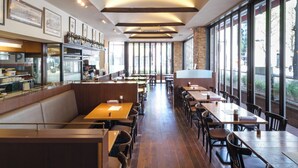 Um restaurante com pisos de madeira, cabines e mesas, janelas amplas e quadros nas paredes.