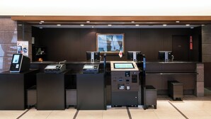 Uma área de recepção moderna com balcão, totens digitais e sala privativa.