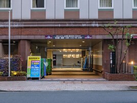 Entrada de hotel com placa de estacionamento, cobertura de passagem e painel de preços do estacionamento.