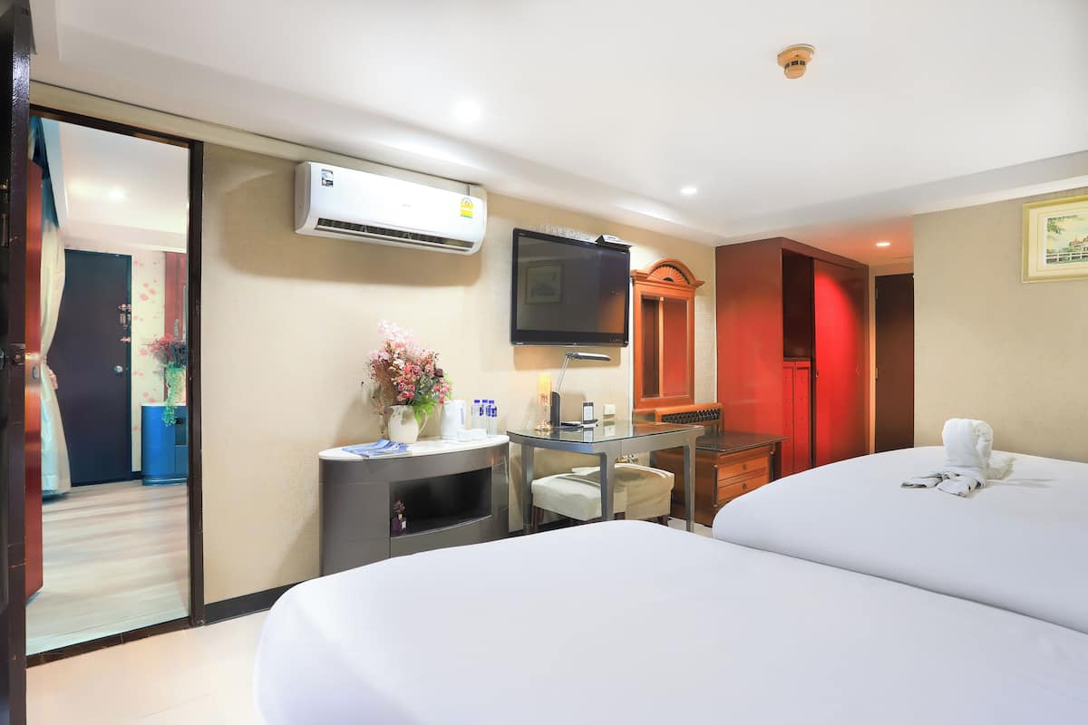 Quarto de hotel com duas camas, uma escrivaninha com cadeira, ar condicionado, televisão e porta com iluminação vermelha.