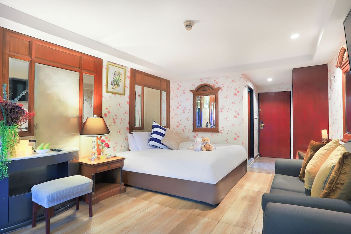 Quarto com cama, mesa de cabeceira, luminária, banqueta e sofá.