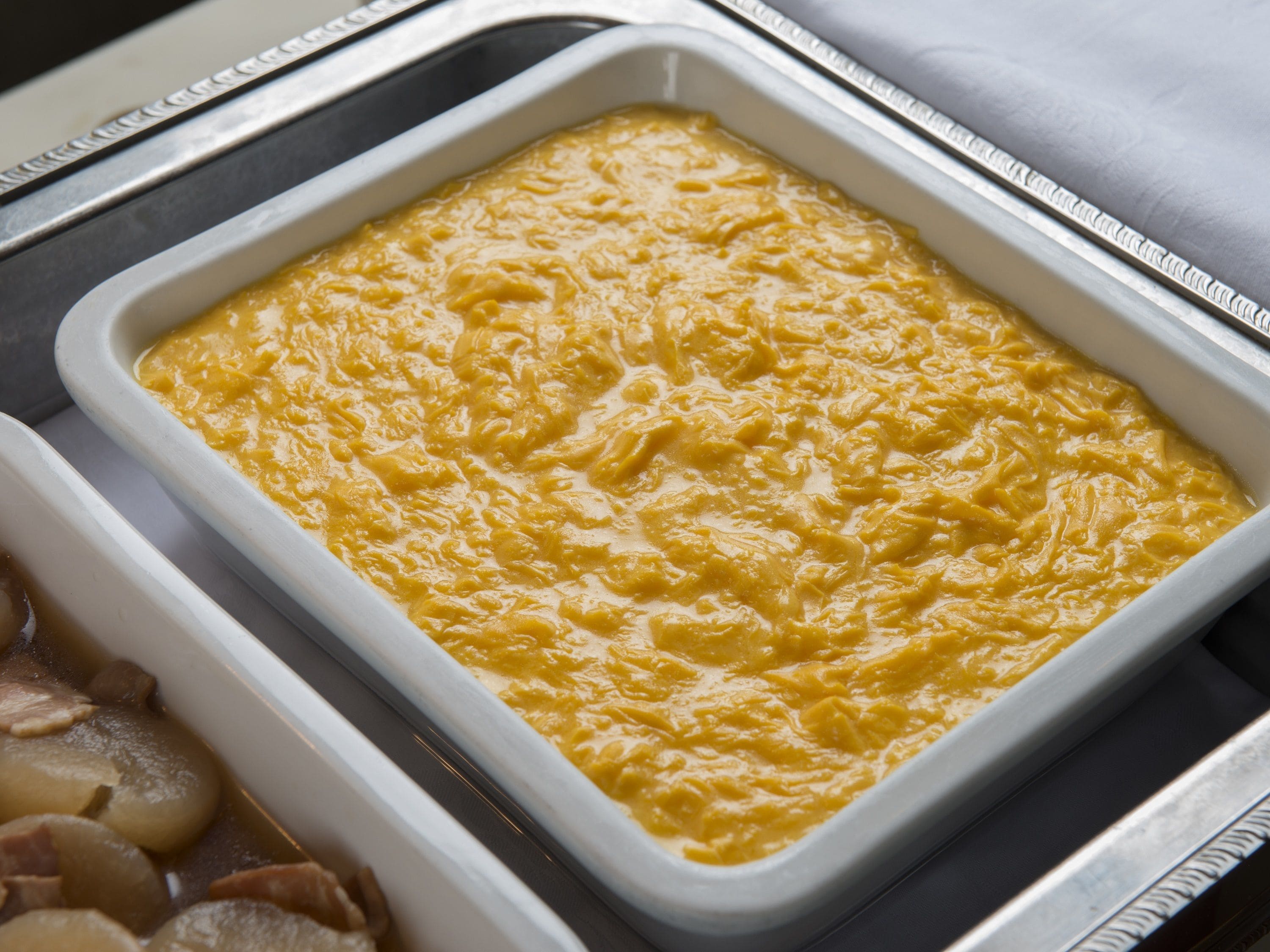 Uma tigela branca retangular com uma substância amarela cremosa, possivelmente uma sobremesa ou um prato assado, sobre uma bandeja.