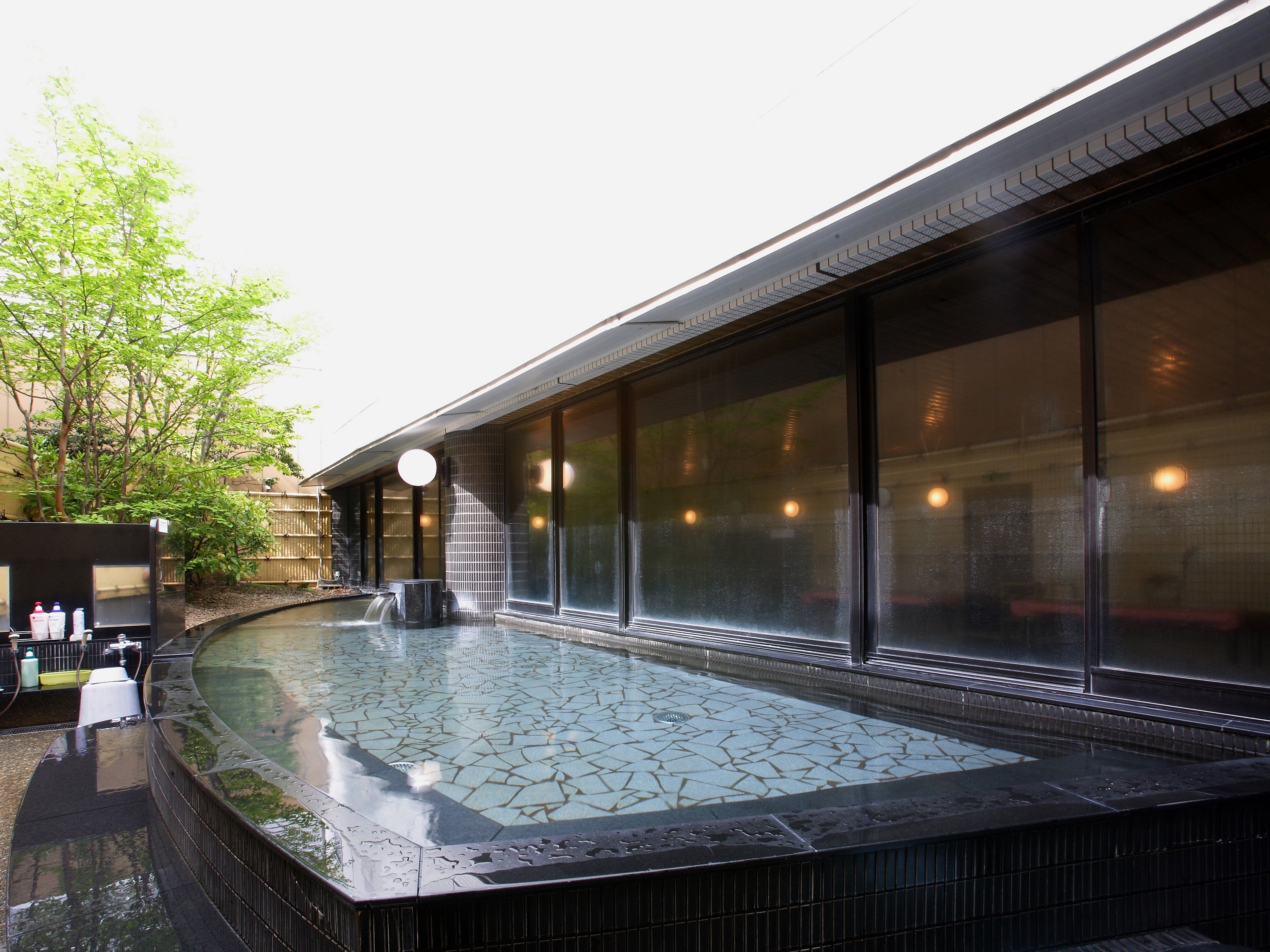 Um edifício moderno com fachada de vidro extensa, piscina com design em mosaico e pequena cascata.