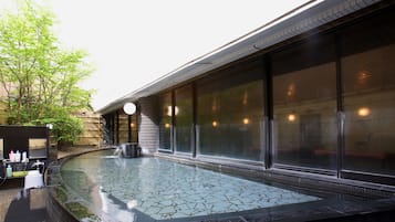 Um edifício moderno com fachada de vidro extensa, piscina com design em mosaico e pequena cascata.