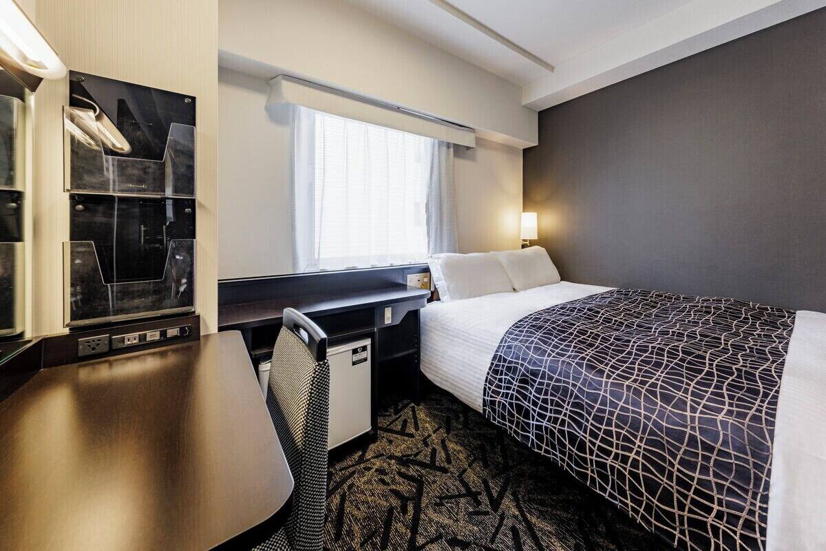 Quarto de hotel com cama, escrivaninha, cadeira e uma pequena cozinha.